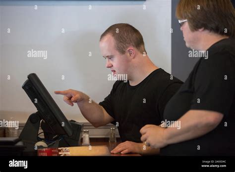 Waiter With Down Syndrome Entering A Sale On Computer With Female