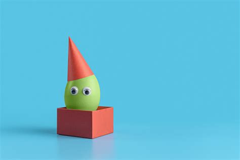 파란색 배경에 사각형 빨간 상자에 빨간 축제 모자에 눈을 가진 하나의 녹색 계란 최소한의 행복 부활절 개념 장식입니다 텍스트 모형의 공간을 복사합니다 0명에 대한 스톡 사진