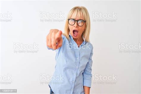 고립 된 흰색 배경 위에 우아한 셔츠와 안경을 착용한 중년 사업가가 카메라에 불쾌하고 좌절하고 화가 나서 분노합니다 가리키기에