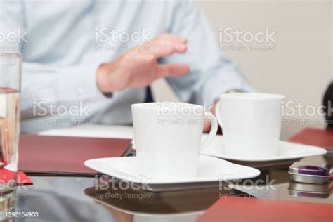 흰색 커피 컵과 접시가있는 유리 테이블 문서 옆에 백그라운드에서 셔츠를 입은 사람 0명에 대한 스톡 사진 및 기타 이미지 0