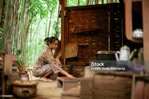 전통적인 케바야와 바틱의 젊은 여성이 자바 주방에서 통나무 나무로 불을 피우고 있다 Javanese Culture에 대한 스톡