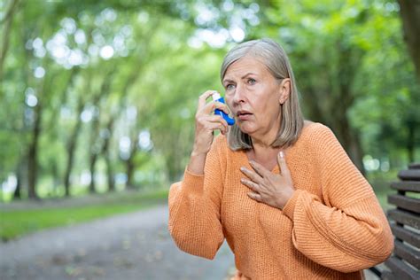 공원 환경에서 천식 흡입기를 사용하는 노인 여성 낮 시간 야외에서 호흡기 문제를 관리하면서 우려를 표명합니다 가을에 대한 스톡 사진 및 기타 이미지 Istock