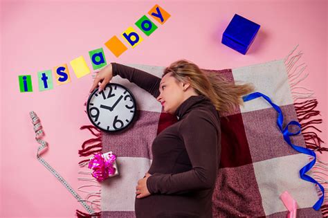 아름다운 임산부는 격자 무늬 포옹 배꼽에 바닥에 누워 시계와 카드를 비문으로 보면 위에서 스튜디오 핑크 배경보기에있는 소년입니다 출산 대기 중 35 39세에 대한 스톡 사진