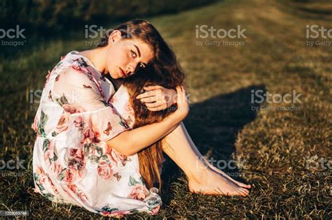 건포도 필드 배경에 긴 곱슬 머리와 아름 다운 여자의 전체 길이 초상화입니다 화창한 날에 가벼운 드레스를 입은 소녀가 잔디에 앉아 있습니다 건강한 생활방식에 대한 스톡 사진