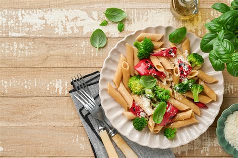 브로콜리와 빨간 구운 피망을 곁들인 통곡물 파스타 펜네와 밝은 나무로 된 소박한 배경 테이블 비건 파스타 전통 이탈리아 요리