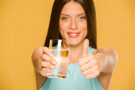 물 한 잔을 들고 노란색 배경에 엄지 손가락을 보여주는 젊은 미소 여자 20 29세에 대한 스톡 사진 및 기타 이미지 20