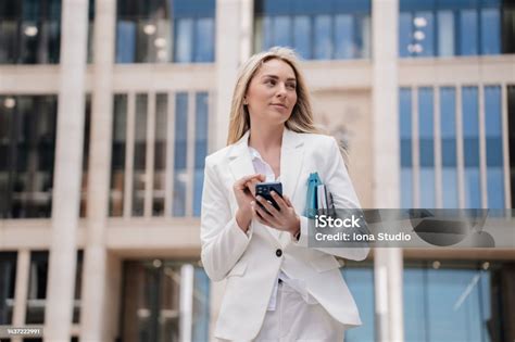 흰 양복을 입은 목적이 있는 젊은 금발 이탈리아 사업가가 사무실에서 성공적으로 일한 후 집으로 돌아가는 것을 옆으로 바라보며 웃고 있다 비즈니스 센터 밖에서 예쁜 여성