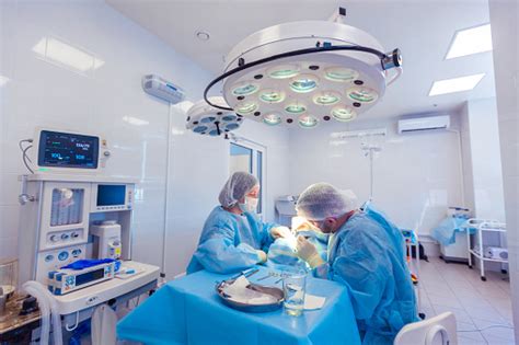 수술실에서 수술을 수행하는 두 명의 외과 의사 옆에 있는 활력 징후 모니터 및 의료 장비 사진 가정의 방에 대한 스톡 사진 및