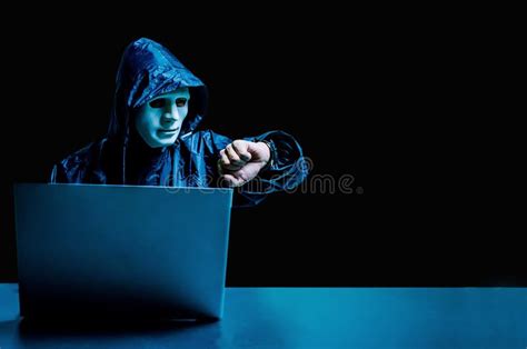Anonymous Computer Hacker In White Mask And Hoodie Obscured Dark Face Using Laptop Computer For