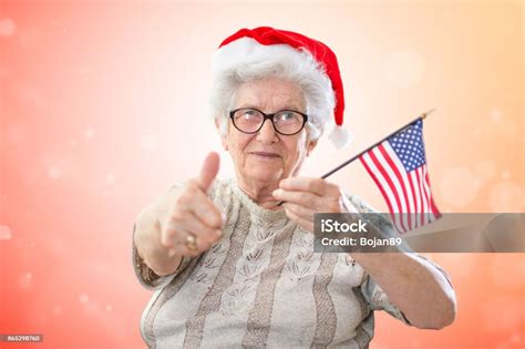 고위 여자 산타의 모자 보여주는 엄지손가락을 착용 하 고 빨간 크리스마스 배경에 대 한 미국 국기를 들고 12월에 대한 스톡 사진 및 기타 이미지 Istock
