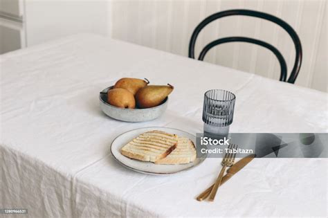 배 과일 구성과 아침 식사 빵 토스트 접힌 신문 흰 린넨 테이블 천에 물 한 잔 최소한의 스칸디나비아 인테리어 배경이 흐려집니다