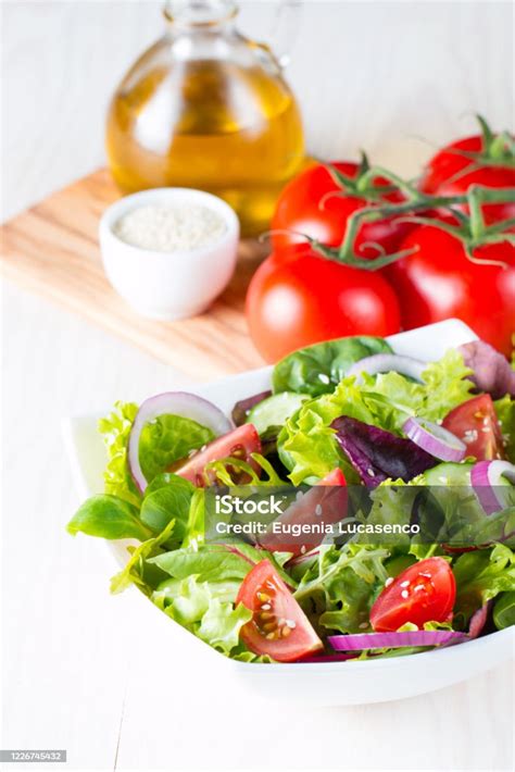 체리 토마토 루콜라 아루굴라 페타 올리브 오이 양파 향신료로 만든 신선한 건강한 야채 샐러드 나무 배경에 흰색 그릇에 그리스어