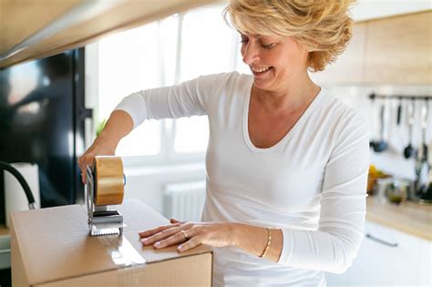 디스펜서에 접착제 테이프와 골판지 상자를 닫는 쾌활한 여자 50 59세에 대한 스톡 사진 및 기타 이미지 50 59세 가정 생활 가정 주방 Istock