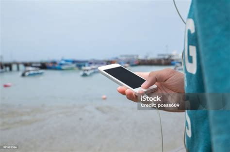 휴대 전화를 사용 하 여 손으로를 닫습니다 부두에서 다리에 이어폰으로 음악을 듣는 동안 스마트폰 들고 맨 손의 세부 사항 거리에
