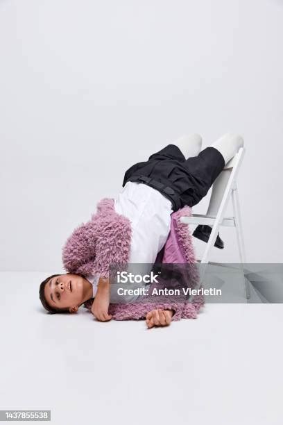 분홍색 모피 코트 흰색 스타킹 검은색 반바지를 입은 세련된 소년의 초상화는 회색 배경 위에 격리된 의자에 누워 있습니다 16 17 살에 대한 스톡 사진 및 기타 이미지