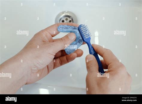 Closeup Of A Man Cleaning His Blue Occlusal Splint Using A Toothbrush In A Bathroom Sink Stock