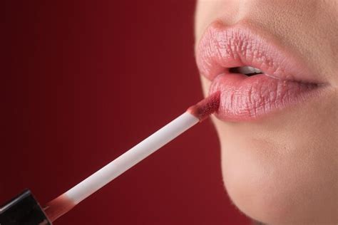 La chica pone lápiz labial en los labios con un primer plano de pincel de los labios de las