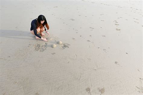 태양을 보호하는 수영복을 입은 여성의 최고 경관은 해변의 모래 위에 앉아 모래와 놀고 성을 건설하고 텍스트를위한 공간을 복사하고