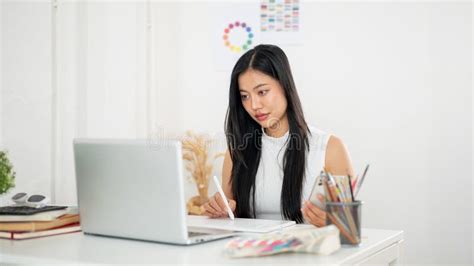 An Asian Woman Is Holding A Stylus Pencil Drawing Or Writing On The Tablet Designer At Work