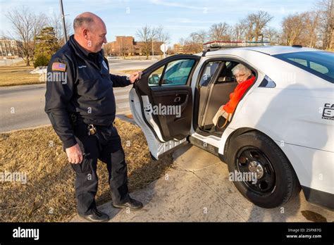 A Police Officer Opens The Door For An Elderly Woman On The Campus Of