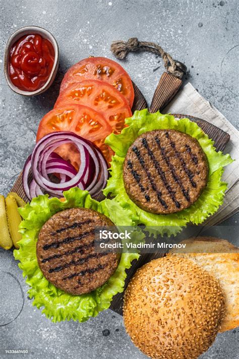 나무 서빙 보드에 비건 구운 패티 토마토 양파를 곁들인 고기 없는 버거를 재배합니다 회색 배경 위쪽 보기 0명에 대한 스톡 사진