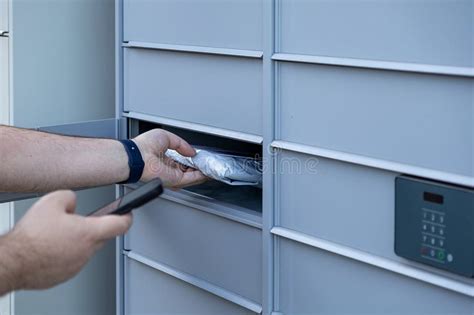 Customer Hand With Smartphone Retrieving Package From Automated Parcel