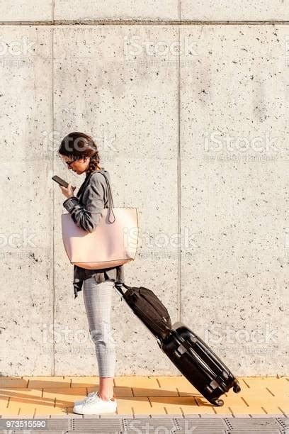 콘크리트 벽 옆에 서 고 그것에 서류 가방을 작은 바퀴 수하물을 들고 그녀의 스마트 휴대 전화를 사용 하 여 젊은 여자 30 34세에 대한 스톡 사진 및 기타 이미지