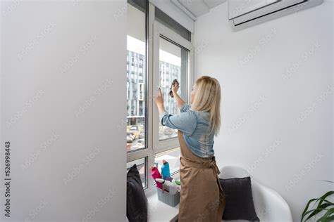 Housewife Sprays The Detergent On The Window And Wipes The Window With A Clean Microfiber Cloth