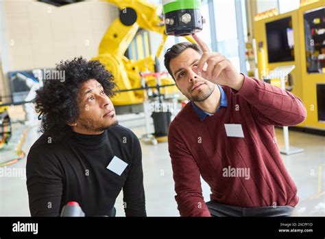 Two Engineers Analyze A Robotic Hand During A Training Session Focused On Industrial Robotics
