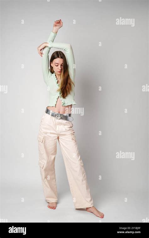 Woman In Green Cardigan And Beige Cargo Pants Poses Against A White