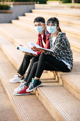 Siswa Lakilaki Dan Perempuan Yang Mengenakan Topeng Duduk Dan Membaca