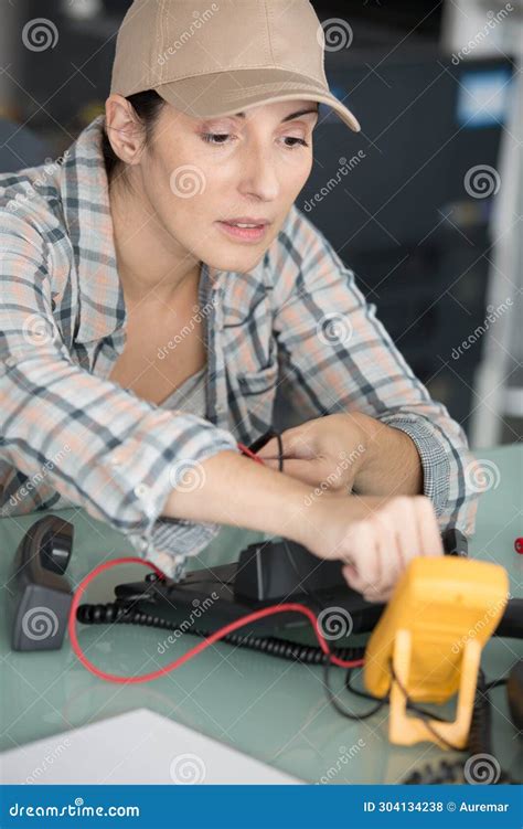 Female Electrician Using Multimeter To Check Telephone Voltage Stock