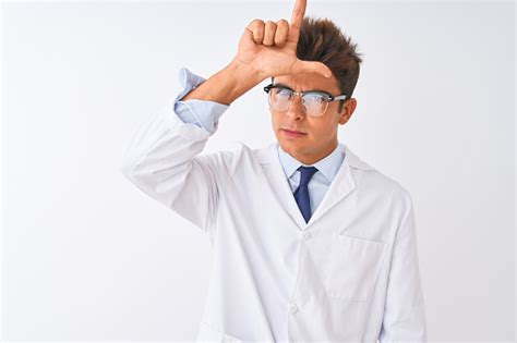 젊은 잘 생긴 Sciencist 남자 안경과 코트 위에 고립 된 흰색 배경 을 통해 이마에 손가락으로 사람들의 재미를 만드는