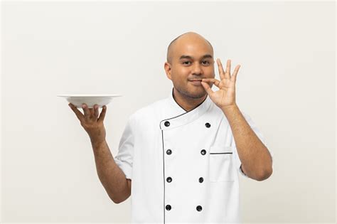 미소 짓는 젊은 잘 생긴 아시아 남자 요리사가 빈 접시를 들고 제복을 입고 맛있는 요리 메뉴를 고립 된 맛있게 만듭니다 인도 남자 요리 직업 요리사 또는 베이커 부엌
