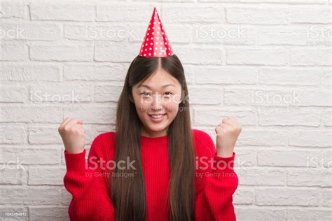 젊은 중국 여자 자랑 비명과 승리와 성공을 매우 흥분된 하 고 축 하 생일 모자를 쓰고 하는 벽돌 벽에 환호 하는 감정 감정에 대한 스톡 사진 및 기타 이미지 Istock