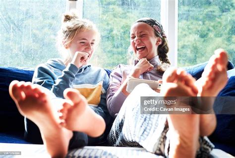Young Girls Sitting On A Couch Looking At A Screen And Laughing High