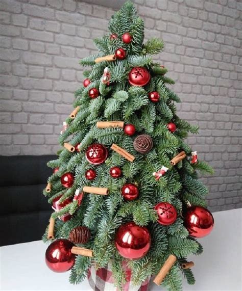 A Small Christmas Tree Decorated With Red Ornaments And Cinnamon Sticks Is Sitting On A Table