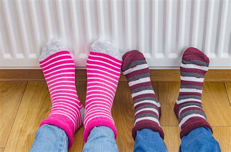 겨울철 난방 라디에이터 앞에서 차가운 발을 따뜻하게 하는 밝은 겨울 양말을 입은 가족 집에서 전기 또는 가스 히터 집에서 난방 시즌의 상징적 인 이미지 가족에 대한 스톡