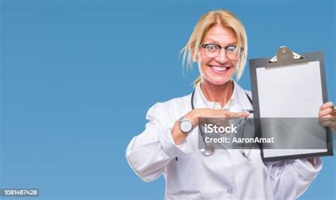 中年金髮碧眼的醫生婦女拿著剪貼簿在孤立的背景非常高興用手和手指指著 照片檔及更多 僅一名女人 照片 僅一名女人 一個人 中老年人