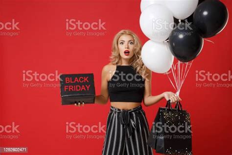 빨간 배경에 고립 포즈 충격 젊은 여자 소녀 발렌타인 데이 여성의 날 생일 컨셉 복사 공간을 모의합니다 검은 색과 금색 선물 상자를 구입 공기 풍선 패키지 가방을 개최합니다