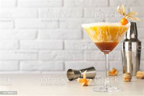 하얀 벽돌 벽 근처의 가벼운 테이블에 Physalis 과일로 장식 된 맛있는 칵테일 텍스트를 위한 공간 바텐더에 대한 스톡 사진