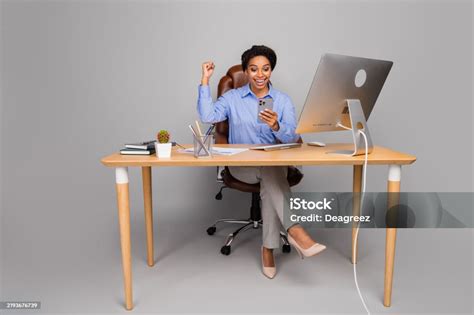 회색 배경에 스마트 폰과 컴퓨터를 가진 사무실 책상에서 온라인 성공을 축하하는 젊은 사업가 25 29세에 대한 스톡 사진 및 기타 이미지 25 29세 Brand