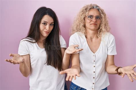Mother And Daughter Standing Together Over Pink Background Clueless And