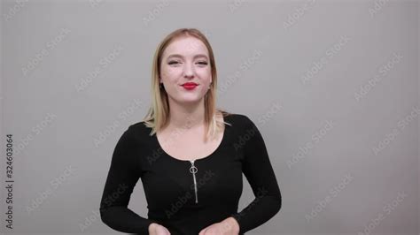 Young Blonde Girl In Black Jacket On Grey Background An Insincere Woman