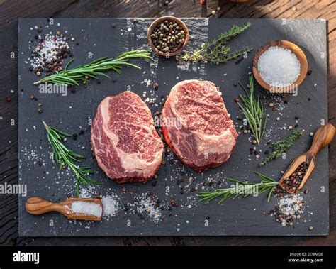 Raw Ribeye Steaks With Salt And Herbs On Grey Board Top View Stock