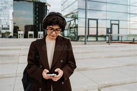 European Woman In Headphones Using Cellphone While Standing On Stairs