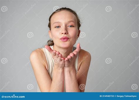 Young Woman Blowing A Kiss While Posing Against A Grey Background