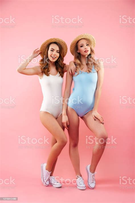 분홍색 배경에 고립 된 사랑스러운 표정과 미소로 포즈를 취하는 화려한 원피스 수영복과 밀짚 모자를 입은 멋진 소녀 20 대의