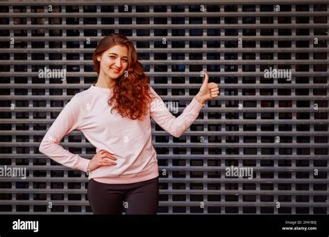 Happy Redhead Girl Shows Us Thumb Up Sign In Front Of Metal Grid Happy