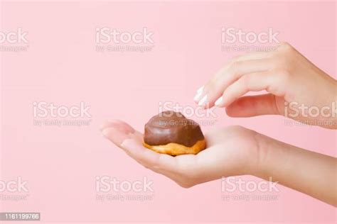 파스텔 핑크 배경에 초콜릿 유약으로 구운 빵을 들고 있는 젊은 여성 과자 에 도달 근접 촬영 측면 뷰 갈색에 대한 스톡 사진 및